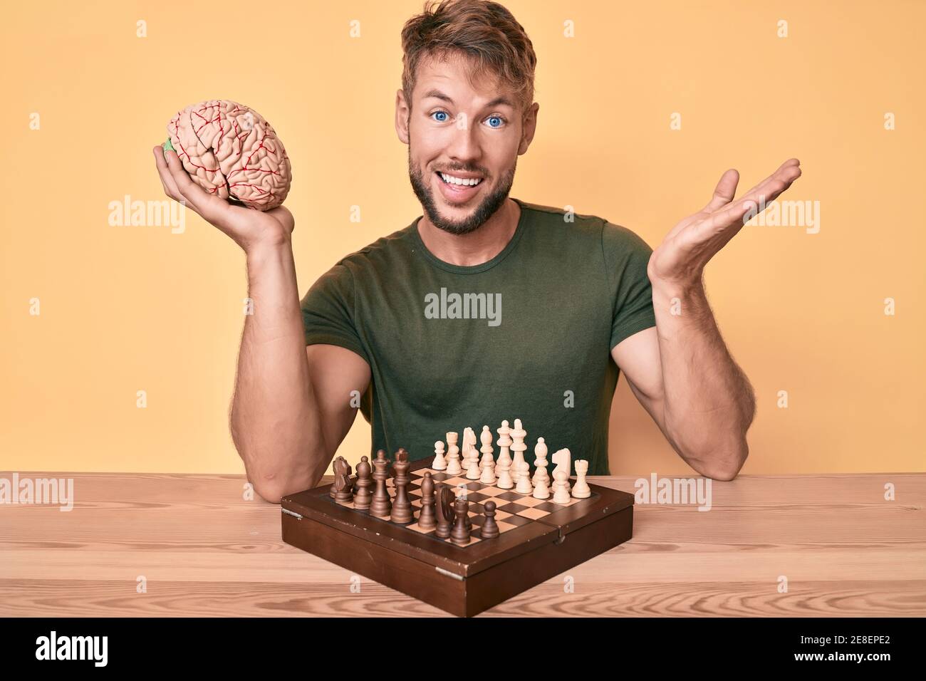 Young caucasian man holding brain while playing chess celebrating ...