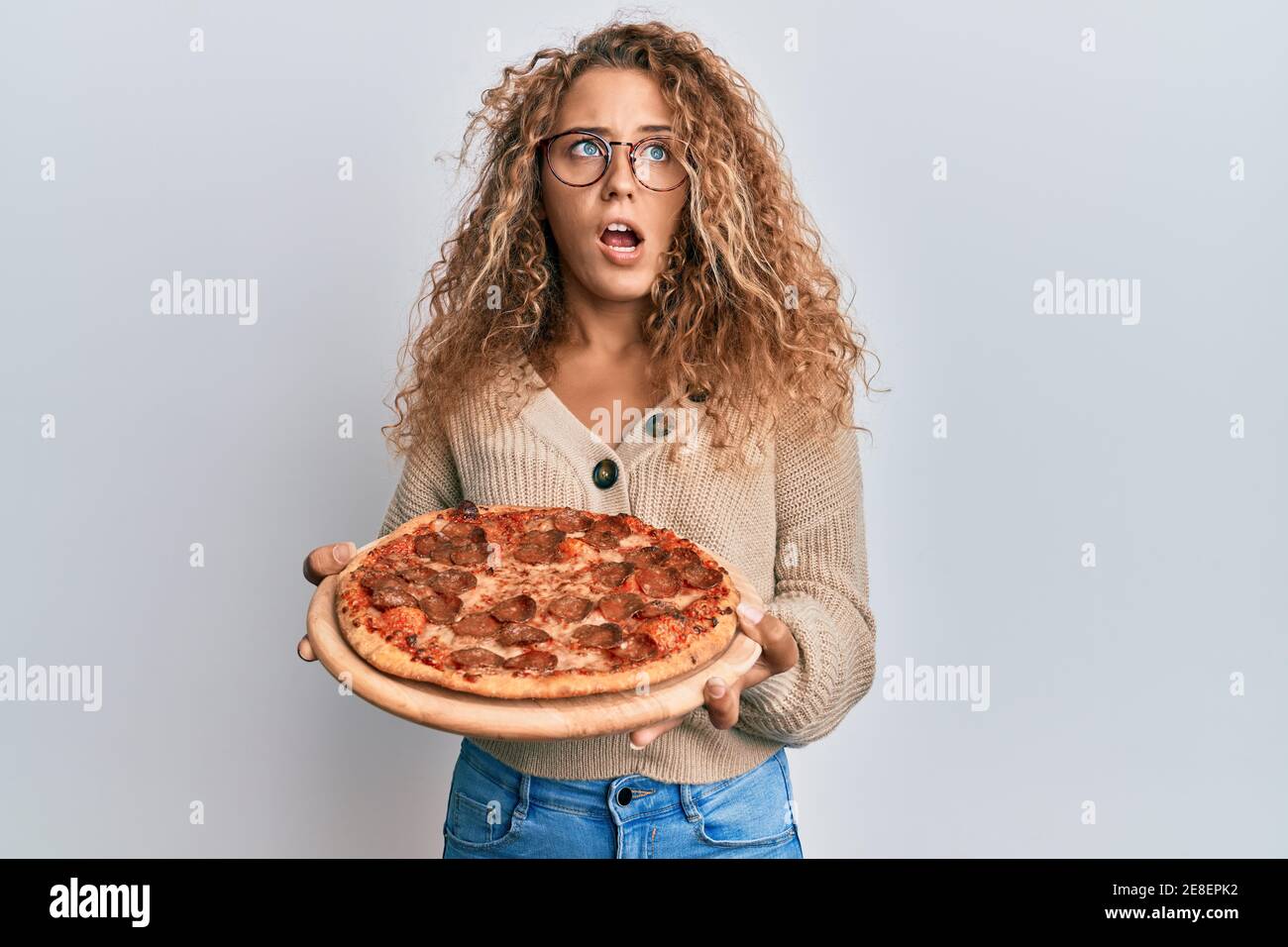Beautiful caucasian teenager girl eating tasty pepperoni pizza angry ...