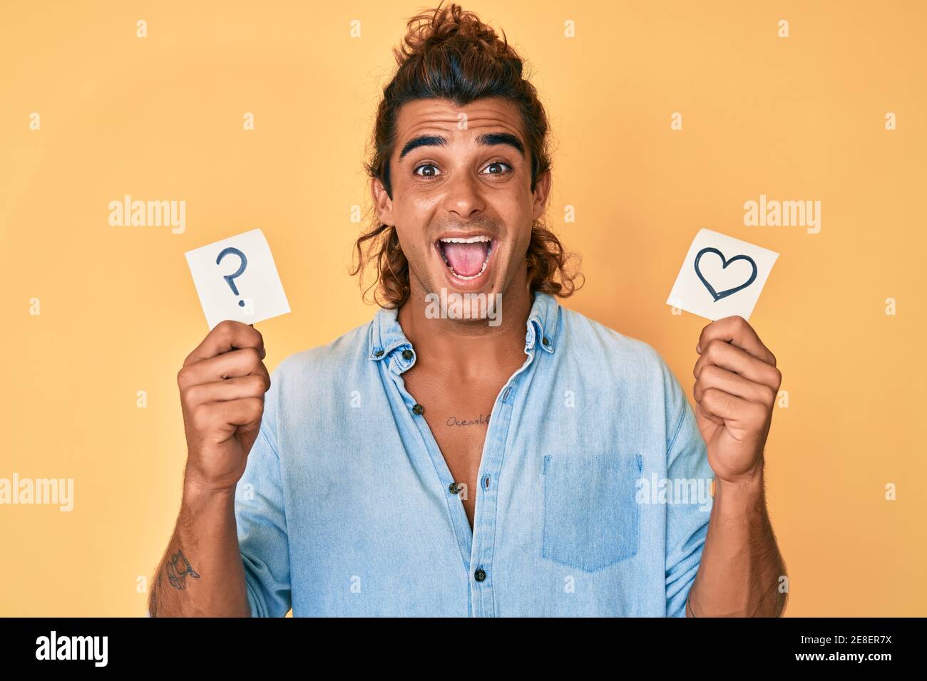 Young hispanic man holding heart and question mark reminder celebrating ...