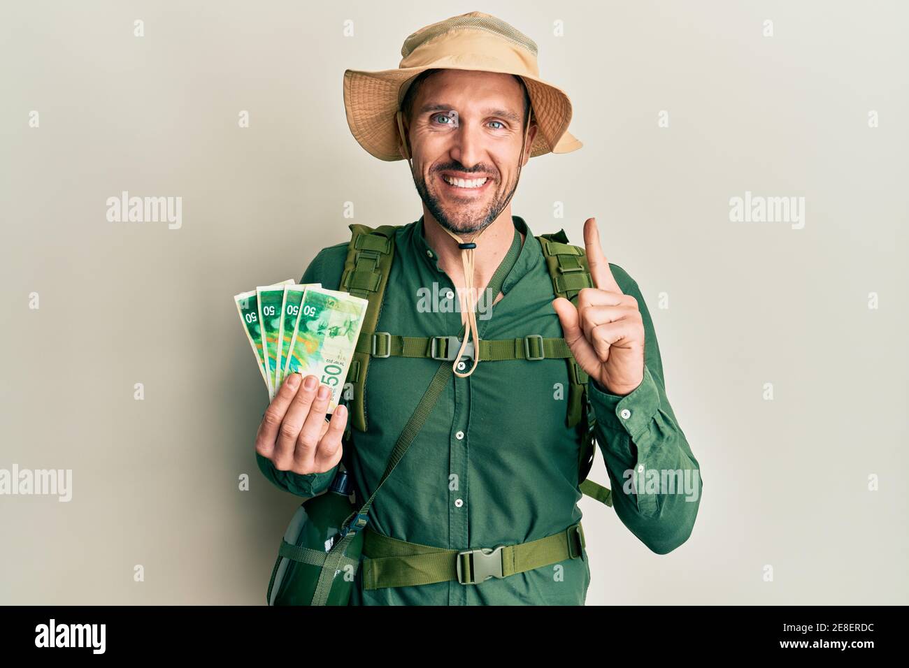 Handsome man with beard wearing explorer hat holding 50 shekels smiling ...