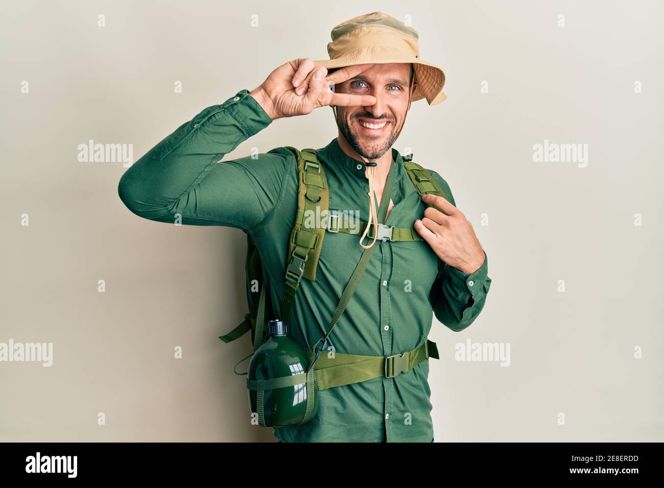 Handsome man with beard wearing explorer hat and backpack doing peace ...