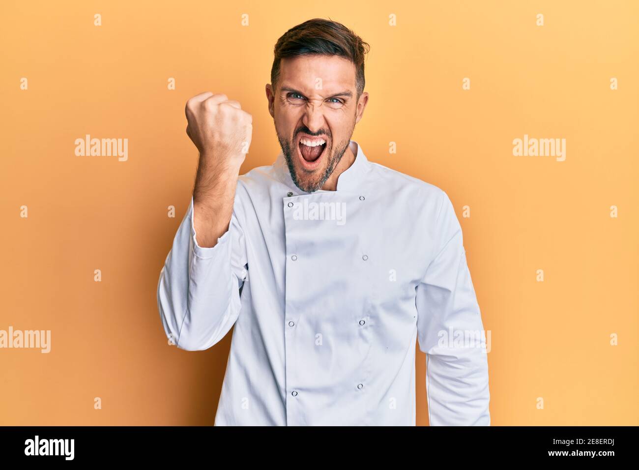 Handsome man with beard wearing professional cook uniform angry and mad ...