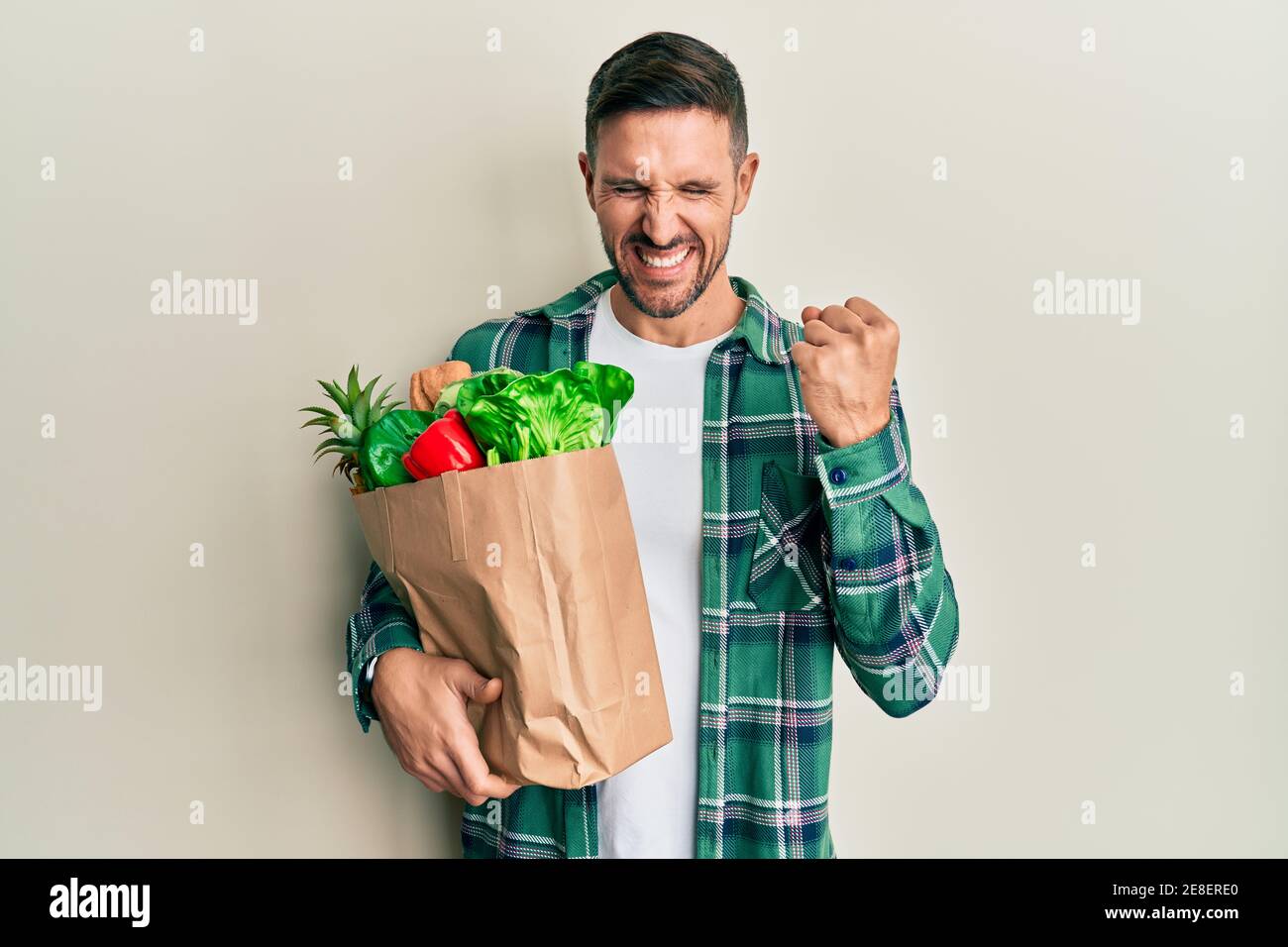 Handsome man with beard holding paper bag with groceries very happy and ...