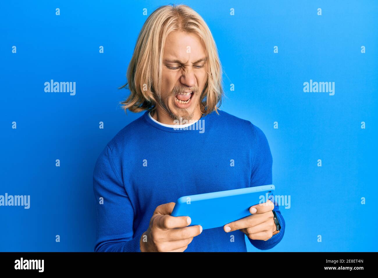 Caucasian young man with long hair using touchpad device angry and mad ...