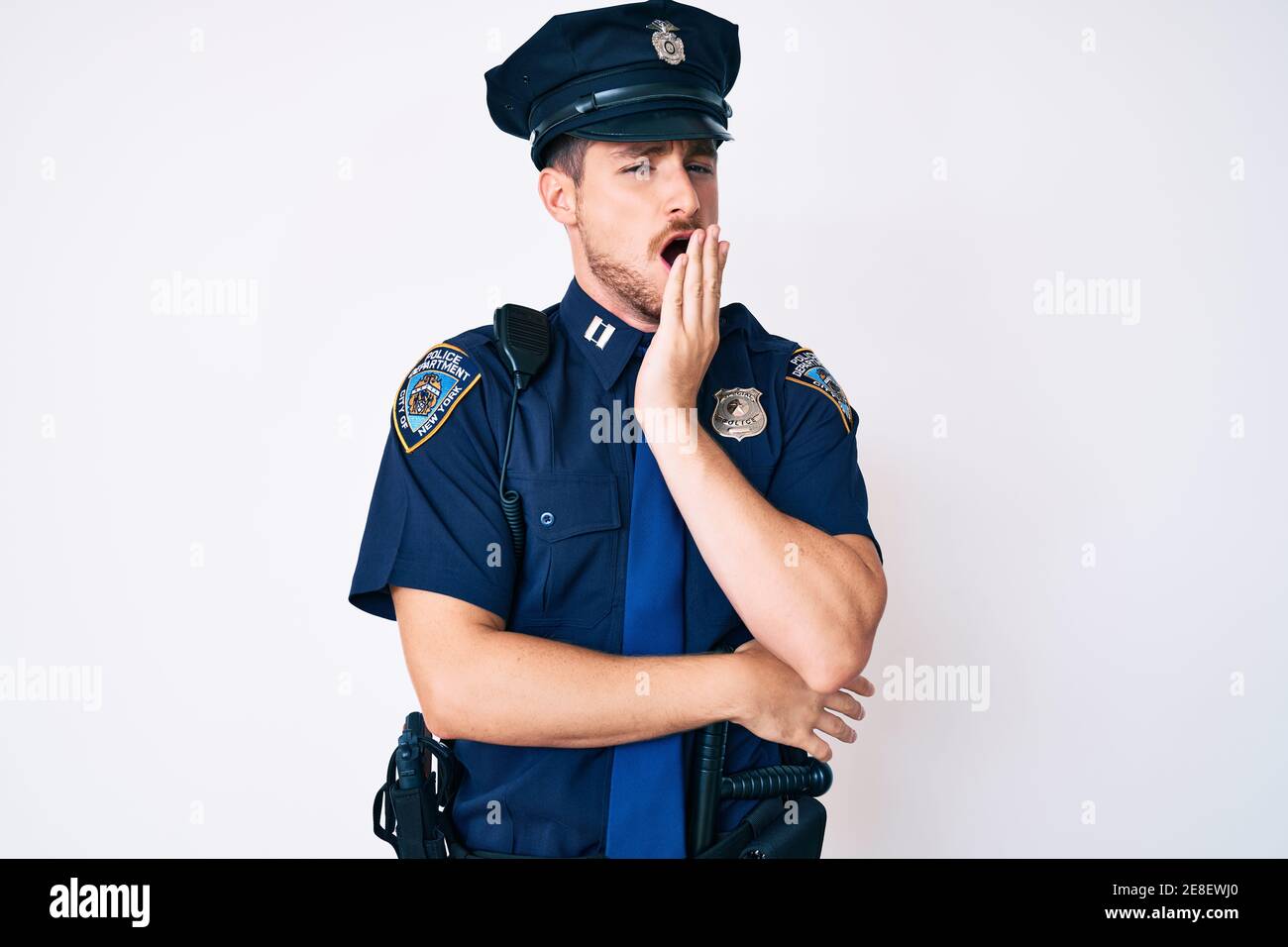 Young caucasian man wearing police uniform bored yawning tired covering ...