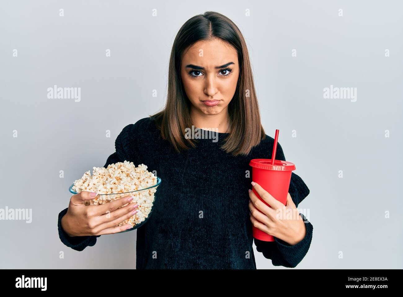 Young brunette girl eating popcorn and drinking soda depressed and ...