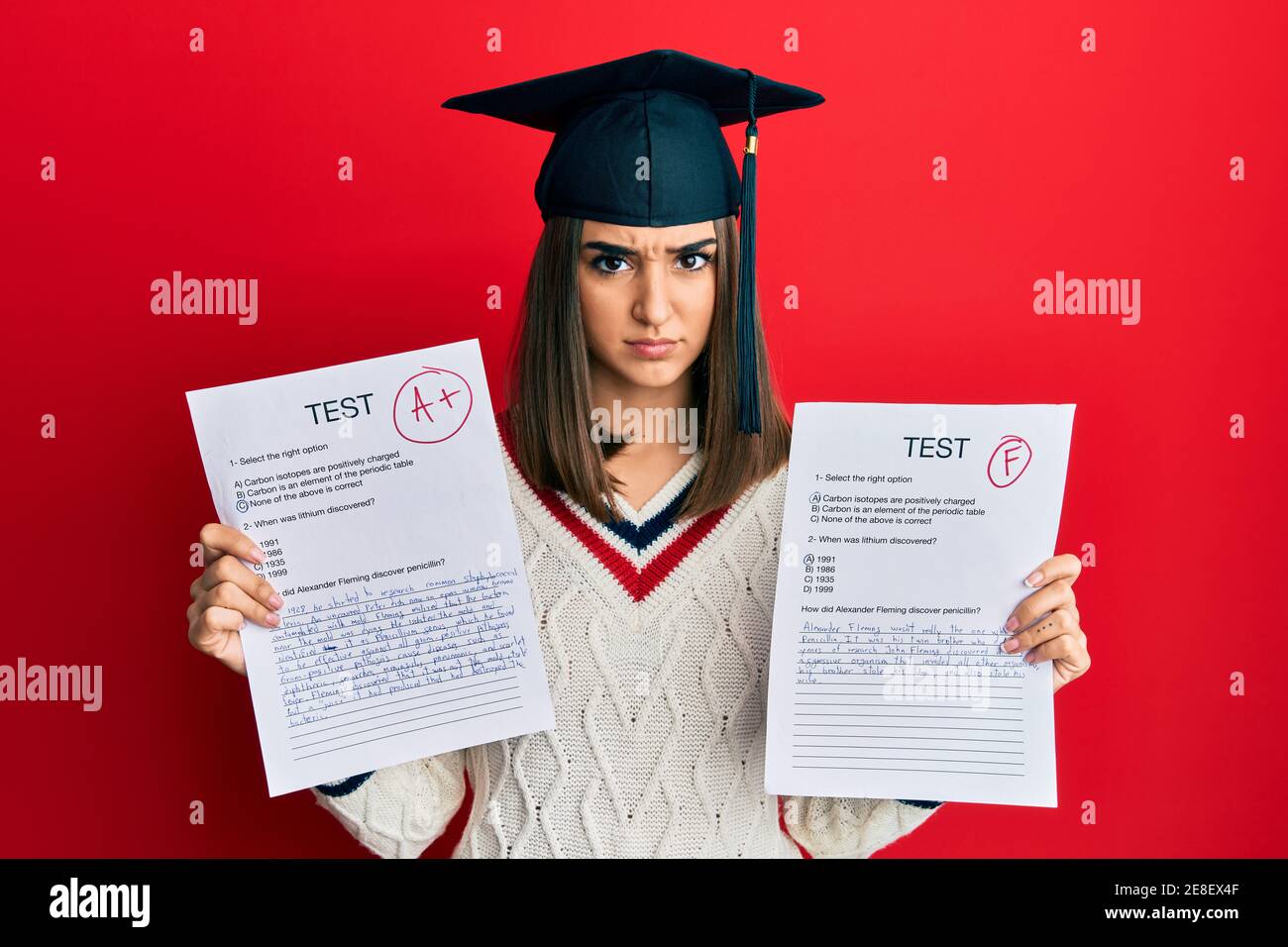Young brunette girl wearing graduation cap showing exams skeptic and ...