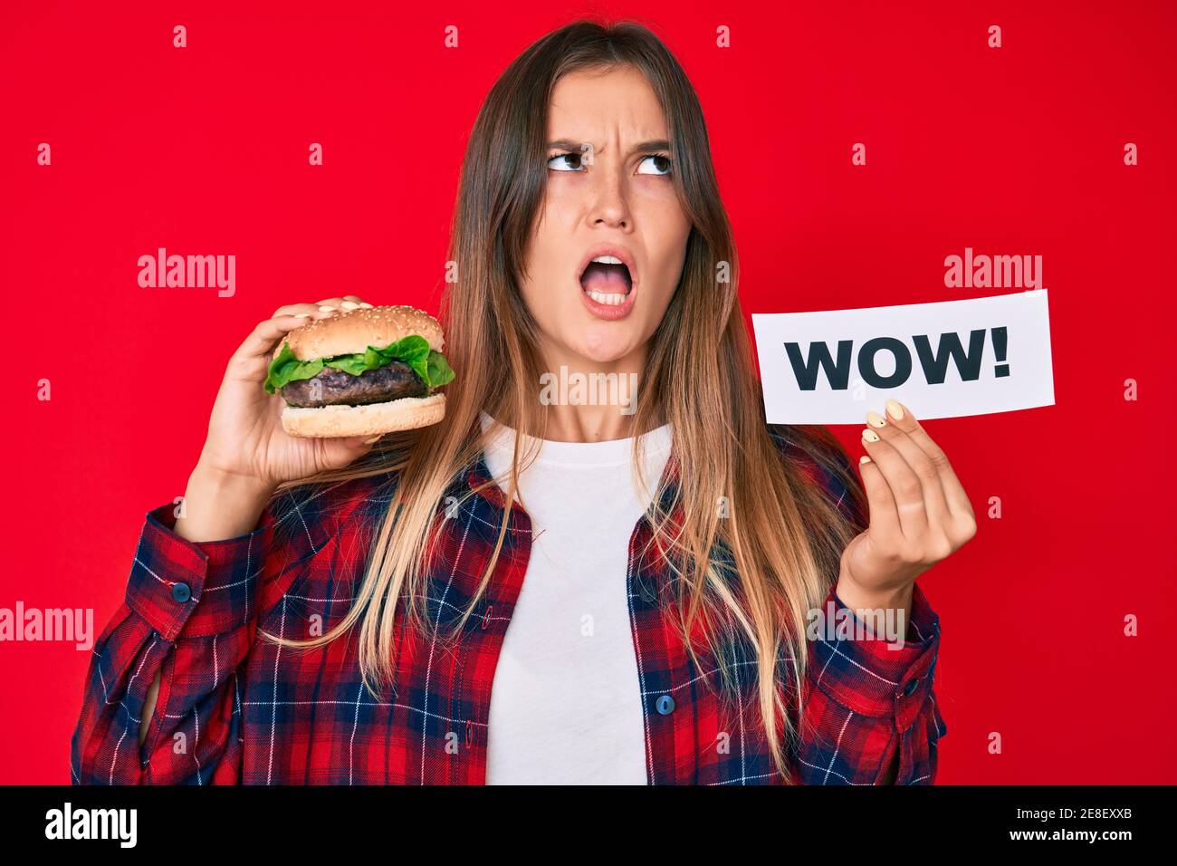 Beautiful caucasian woman eating a tasty classic burger holding wow ...