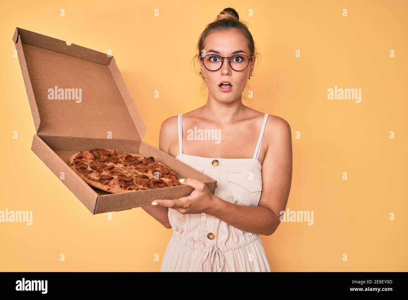 Beautiful caucasian woman holding tasty pepperoni pizza in shock face ...