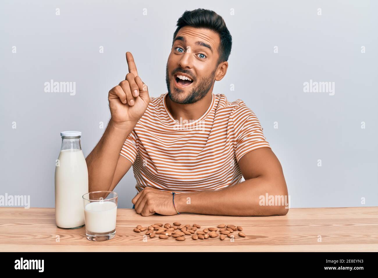 Handsome hispanic man drinking healthy almond milk smiling with an idea ...