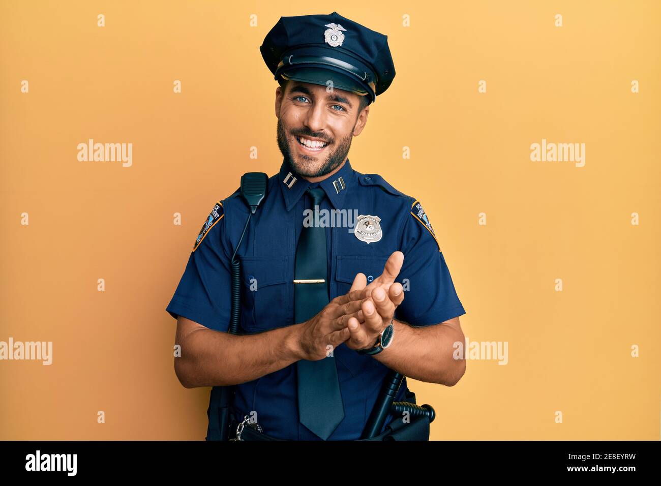Handsome hispanic man wearing police uniform clapping and applauding ...