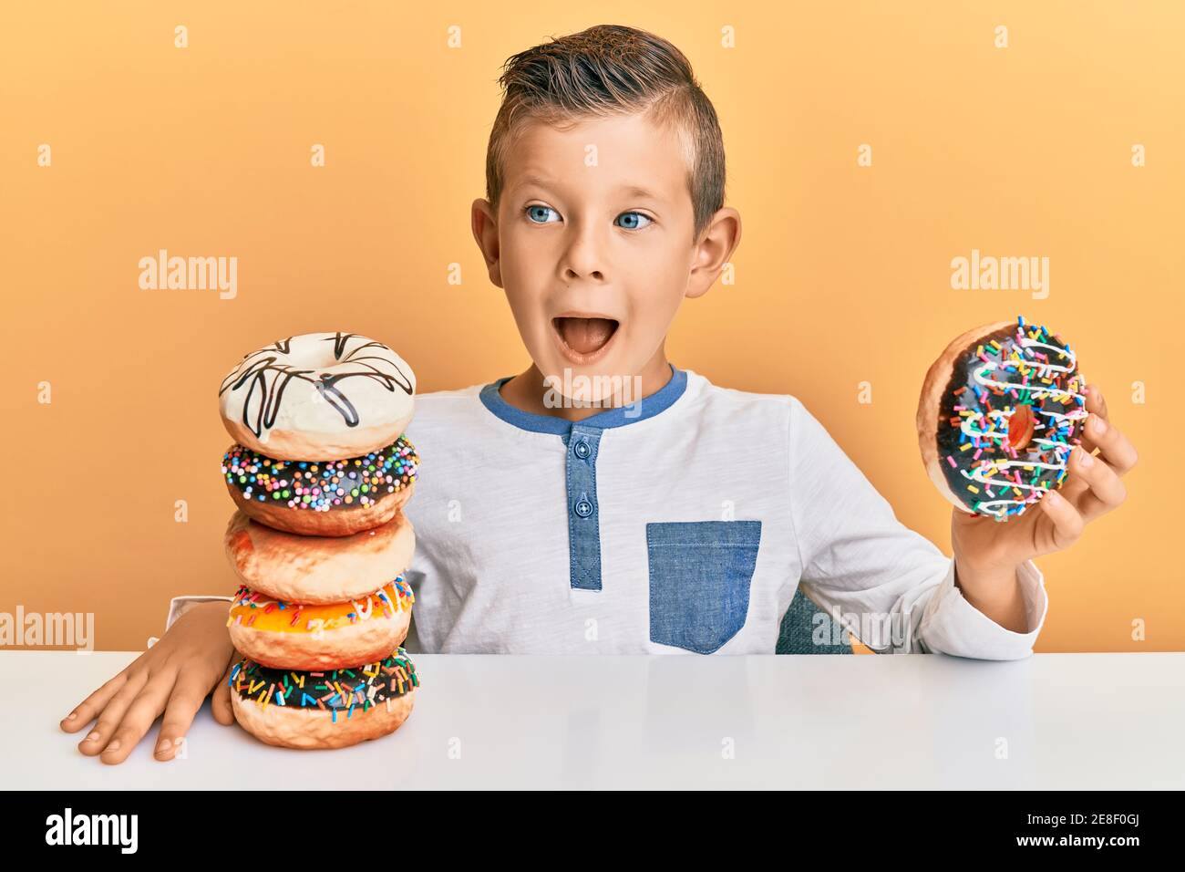 Adorable caucasian kid eating doughnuts for breakfast celebrating crazy ...