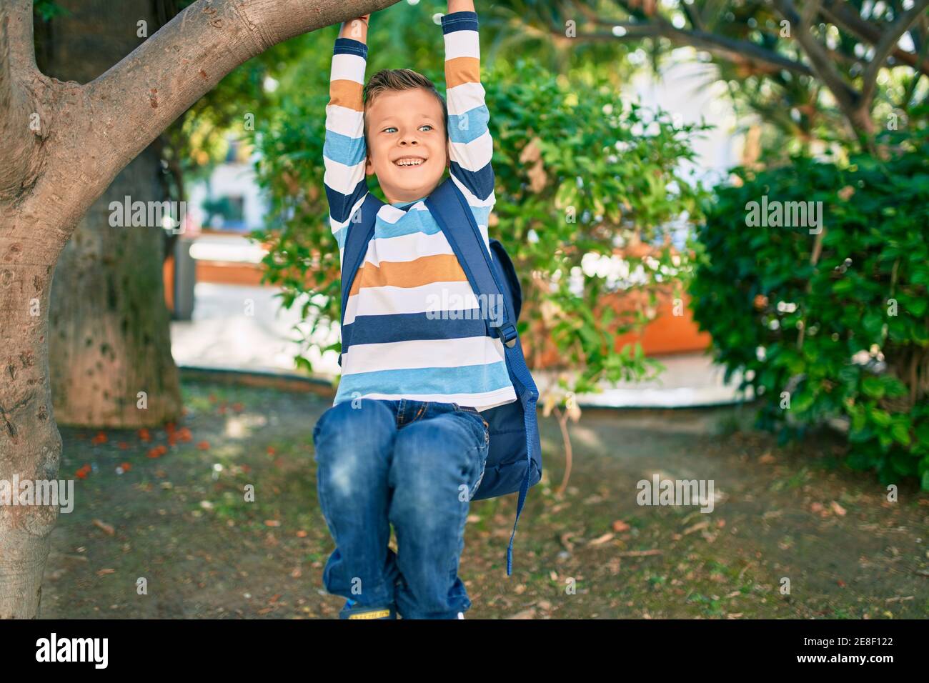 Adorable caucasian student boy smiling happy hanging on tree branch at ...
