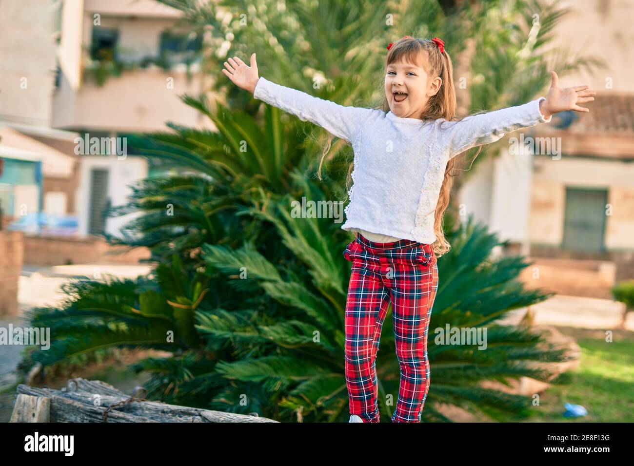 Adorable caucasian child girl with open arms smiling happy at the city ...
