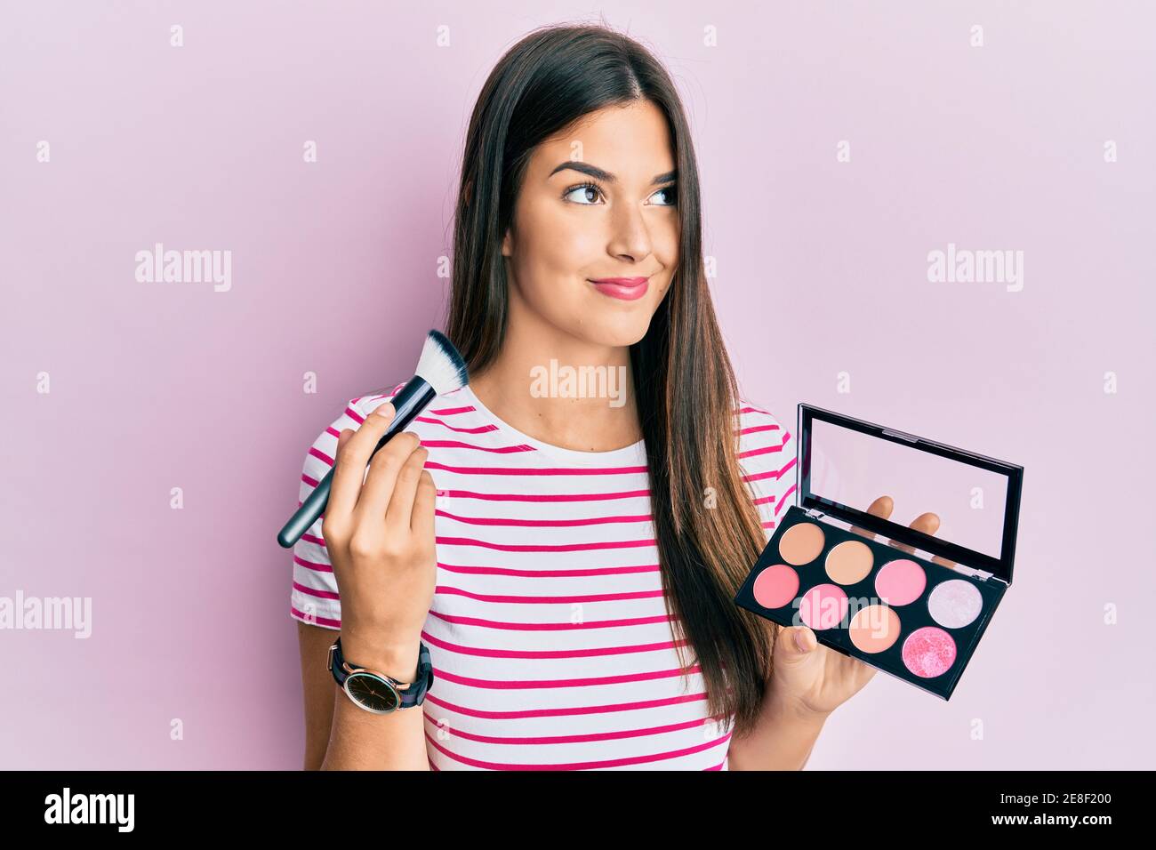 Young brunette woman holding makeup brush and blush palette smiling ...