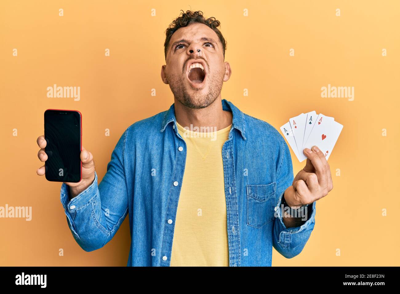 Young hispanic man holding poker cards and smartphone showing blank ...