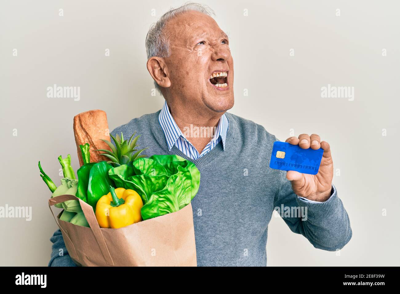 Senior caucasian man holding groceries and credit card angry and mad ...