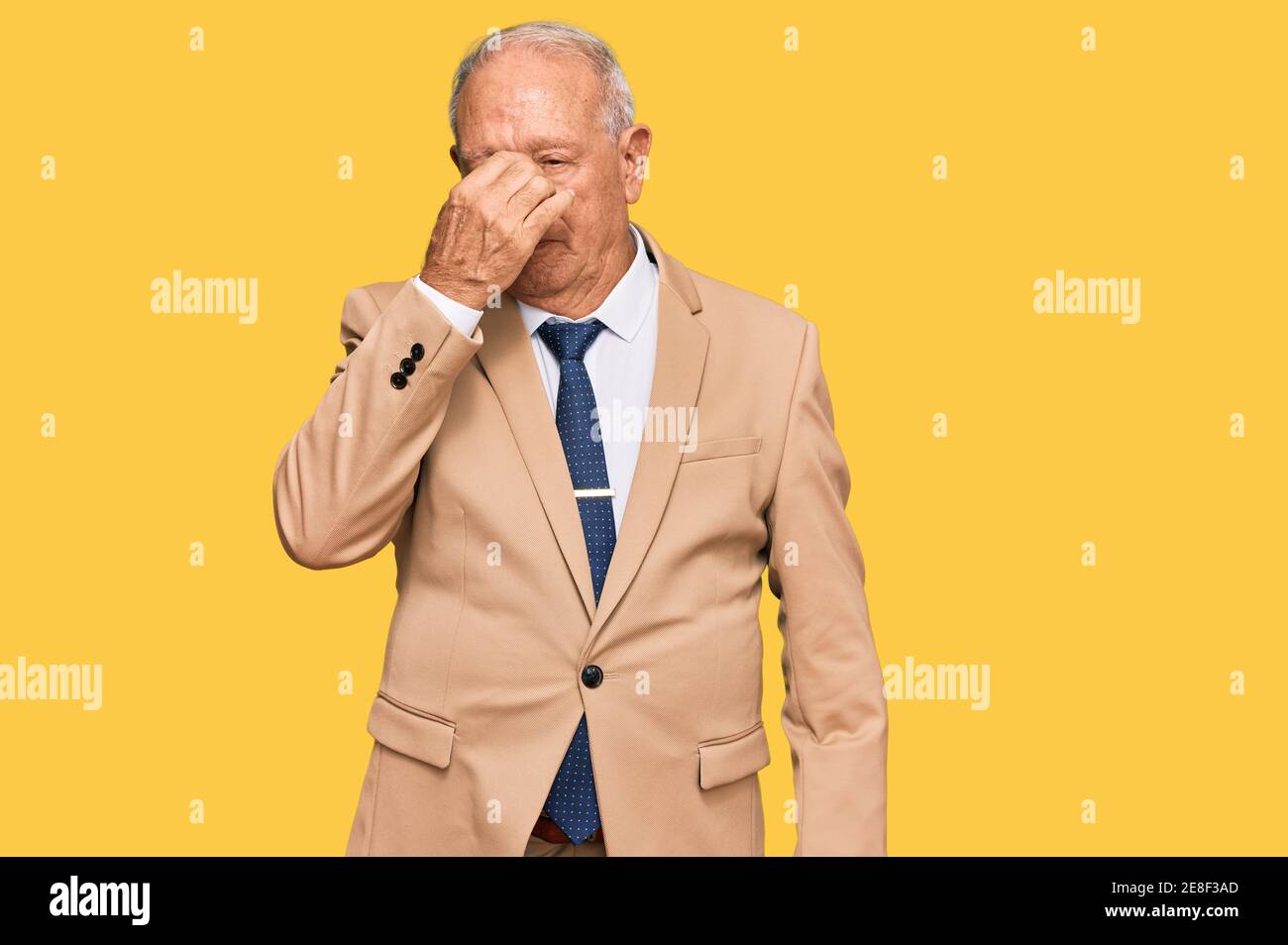 Senior caucasian man wearing business suit and tie tired rubbing nose ...