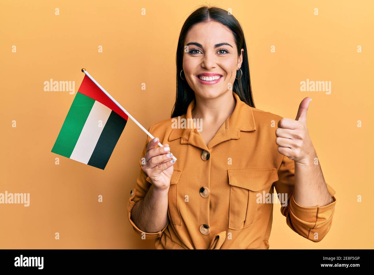 Young brunette woman holding united arab emirates flag smiling happy ...