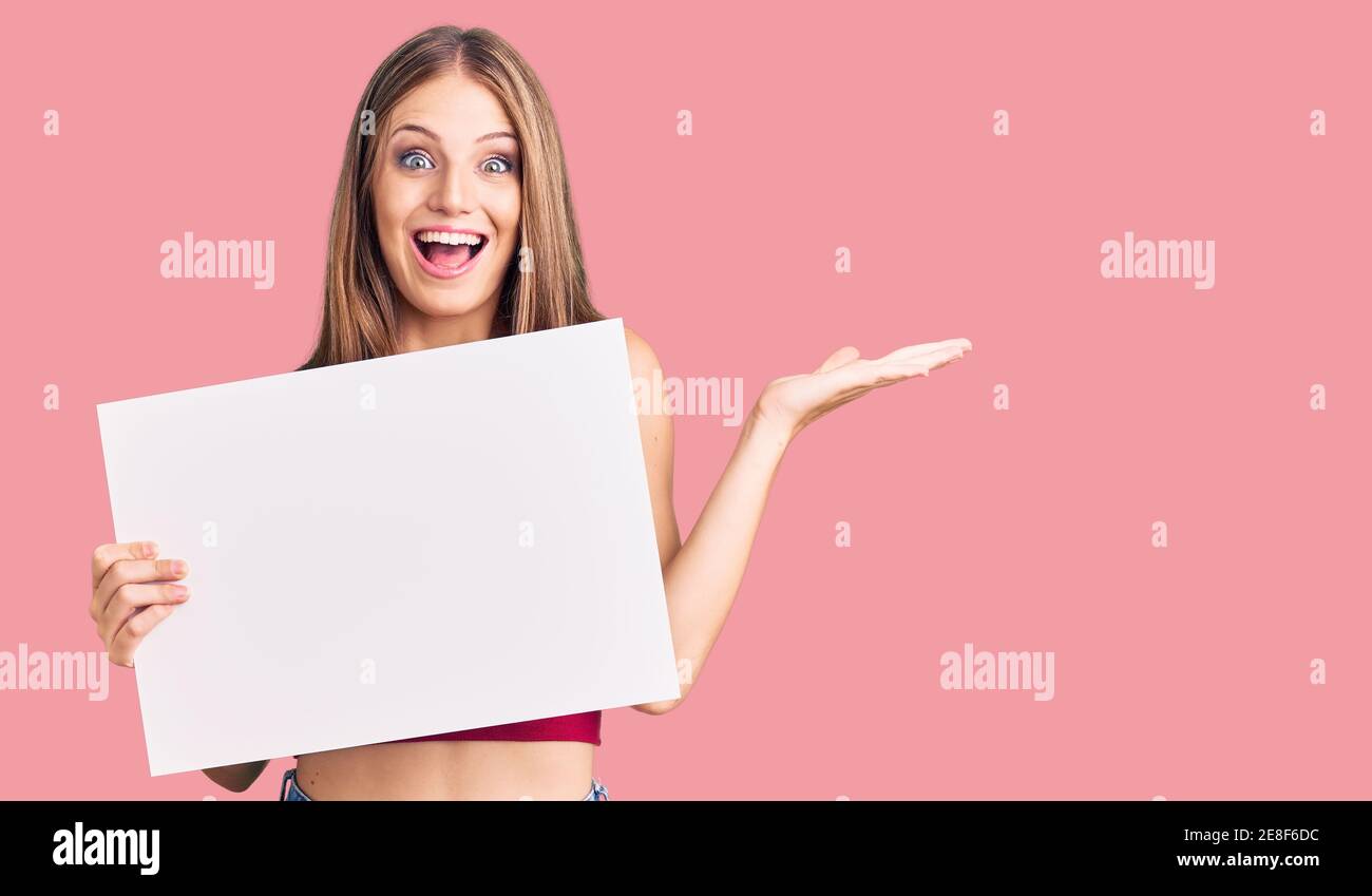 Young beautiful blonde woman holding blank empty banner celebrating ...
