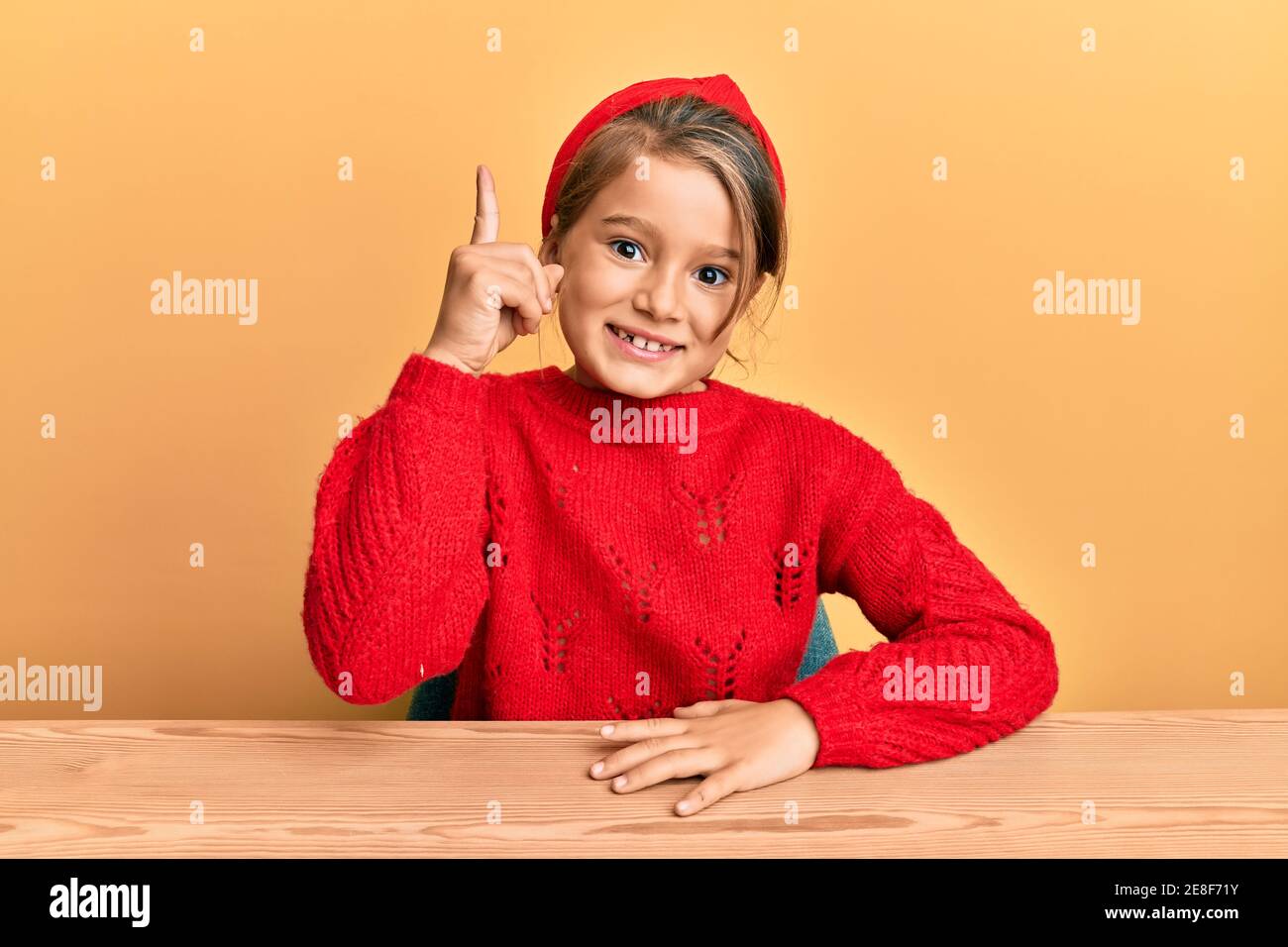 Little beautiful girl wearing casual clothes sitting on the table ...