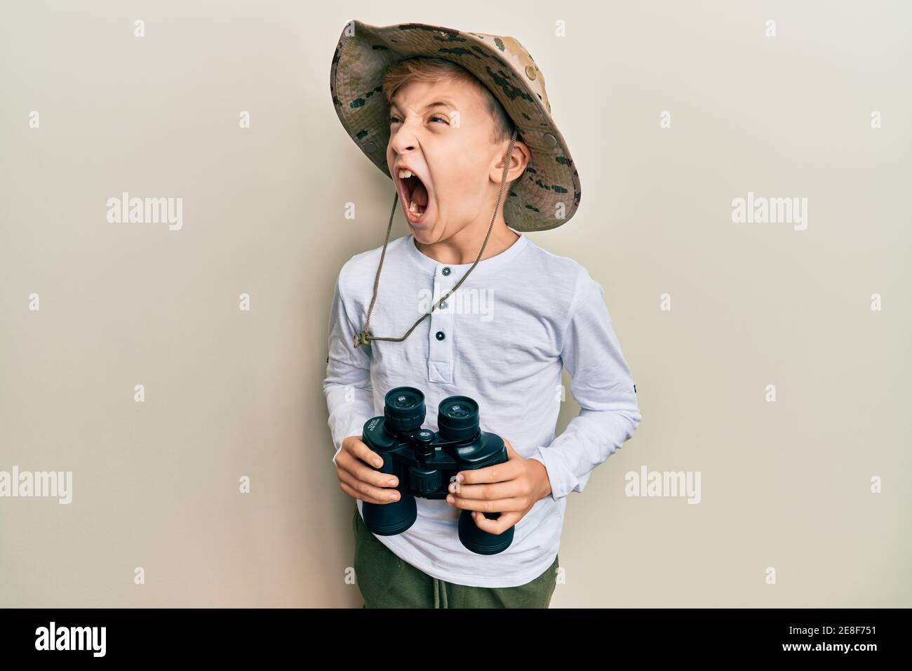 Little caucasian boy kid wearing explorer hat holding binoculars angry ...