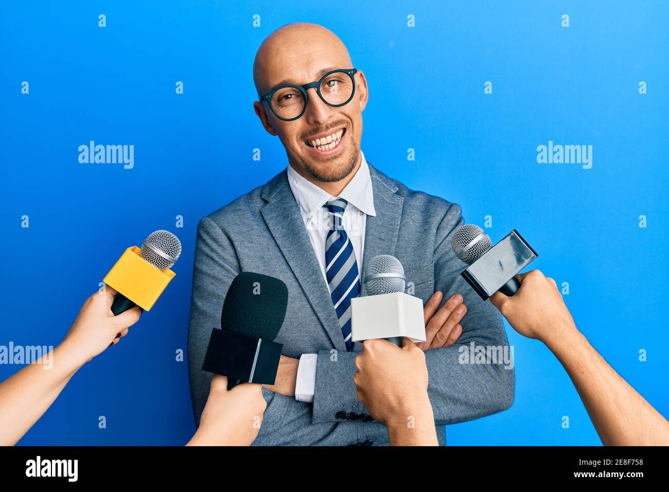 Bald man with beard being interviewed by reporters holding microphones ...