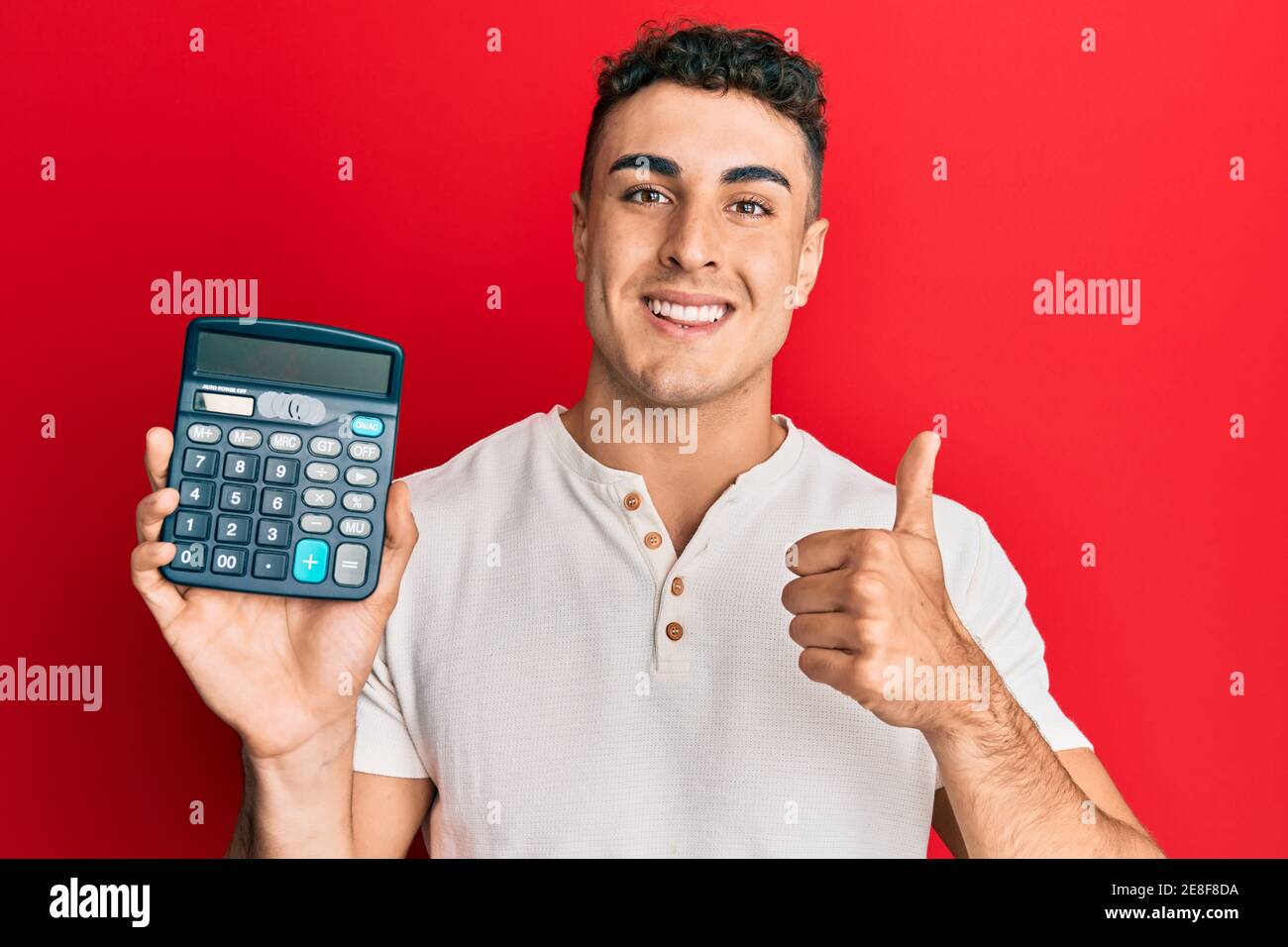 Hispanic young man showing calculator device smiling happy and positive ...