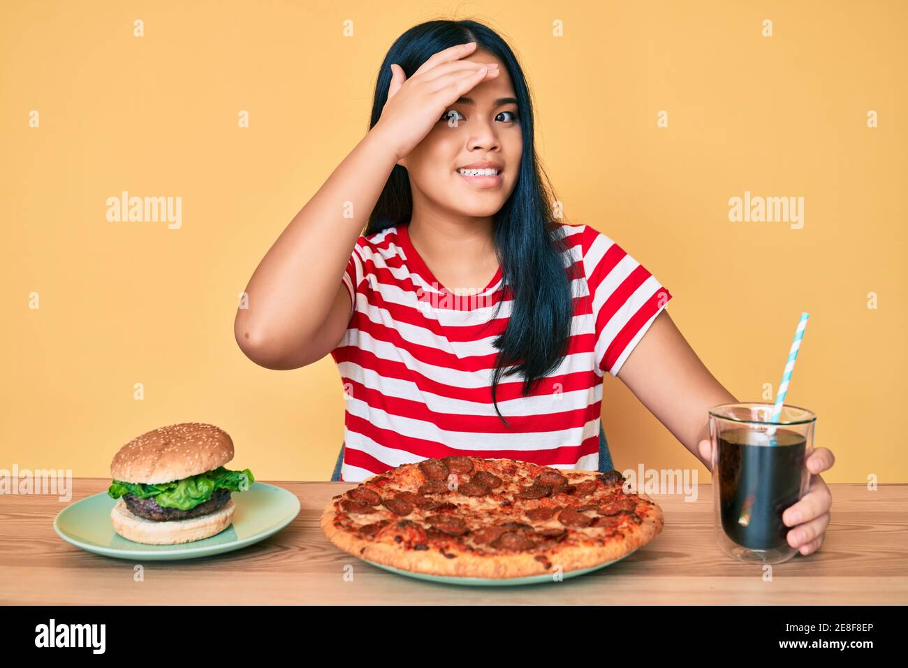 Young beautiful asian girl eating fast food pizza and burger stressed ...