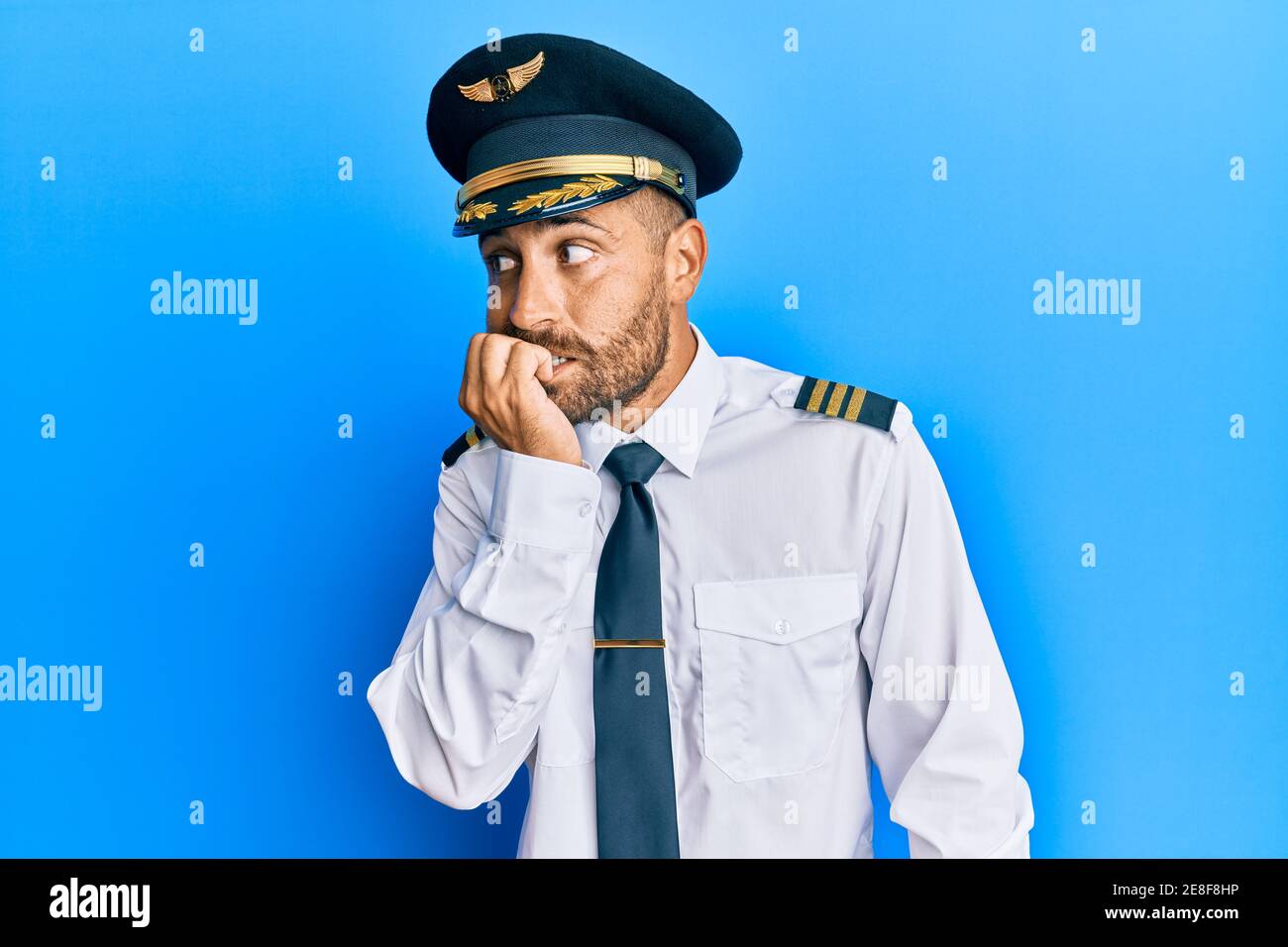 Handsome man with beard wearing airplane pilot uniform looking stressed ...
