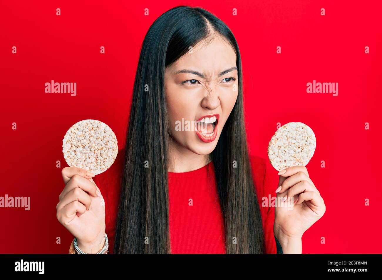 Young chinese woman eating healthy rice crackers angry and mad ...