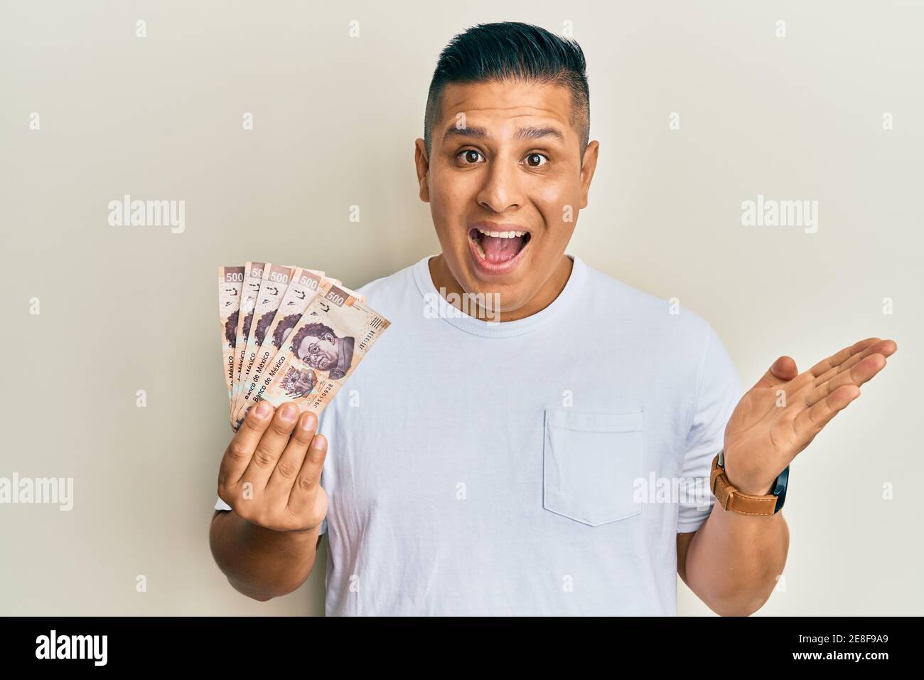 Young latin man holding 500 mexican pesos banknotes celebrating ...