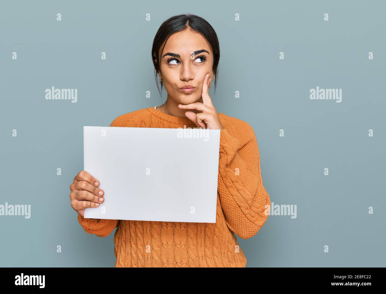 Young brunette woman holding blank empty banner serious face thinking ...