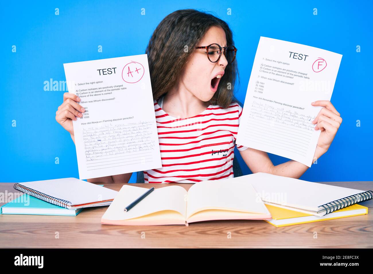 Cute hispanic girl showing failed and passe exam sitting on the table ...