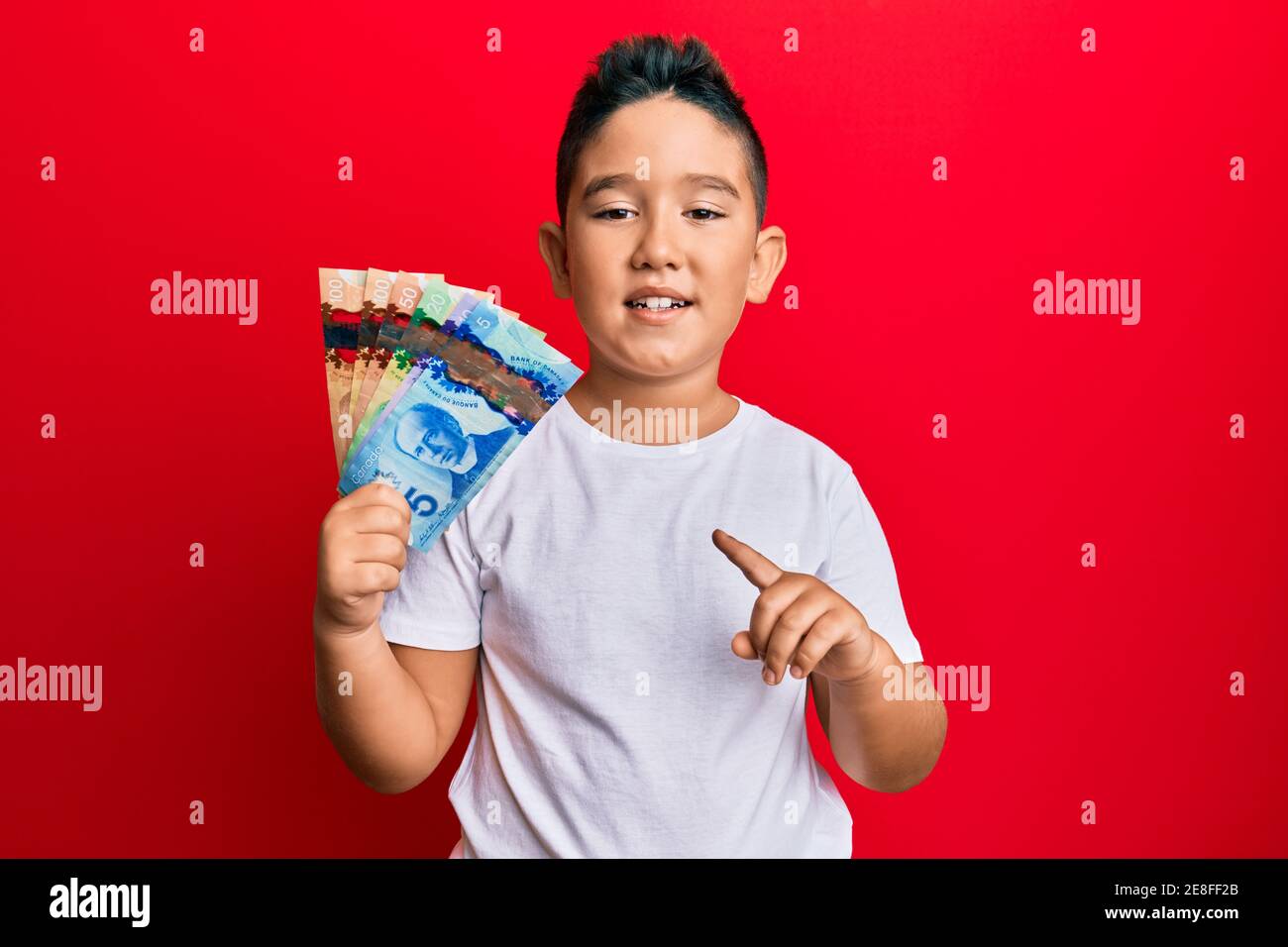 Little boy hispanic kid holding canadian dollars smiling happy pointing ...