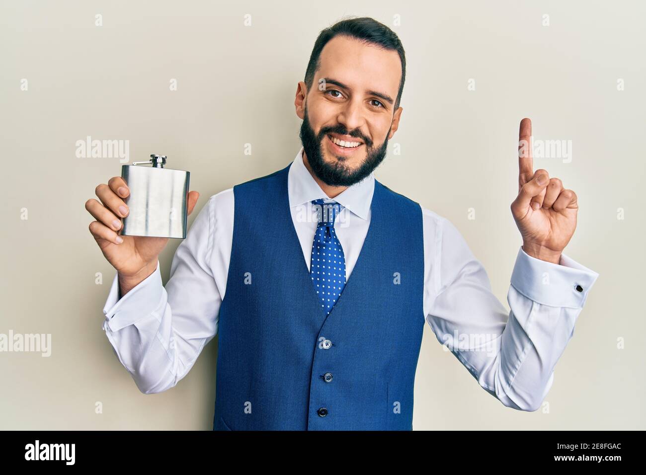 Young man with beard drinking whiskey from flask surprised with an idea ...