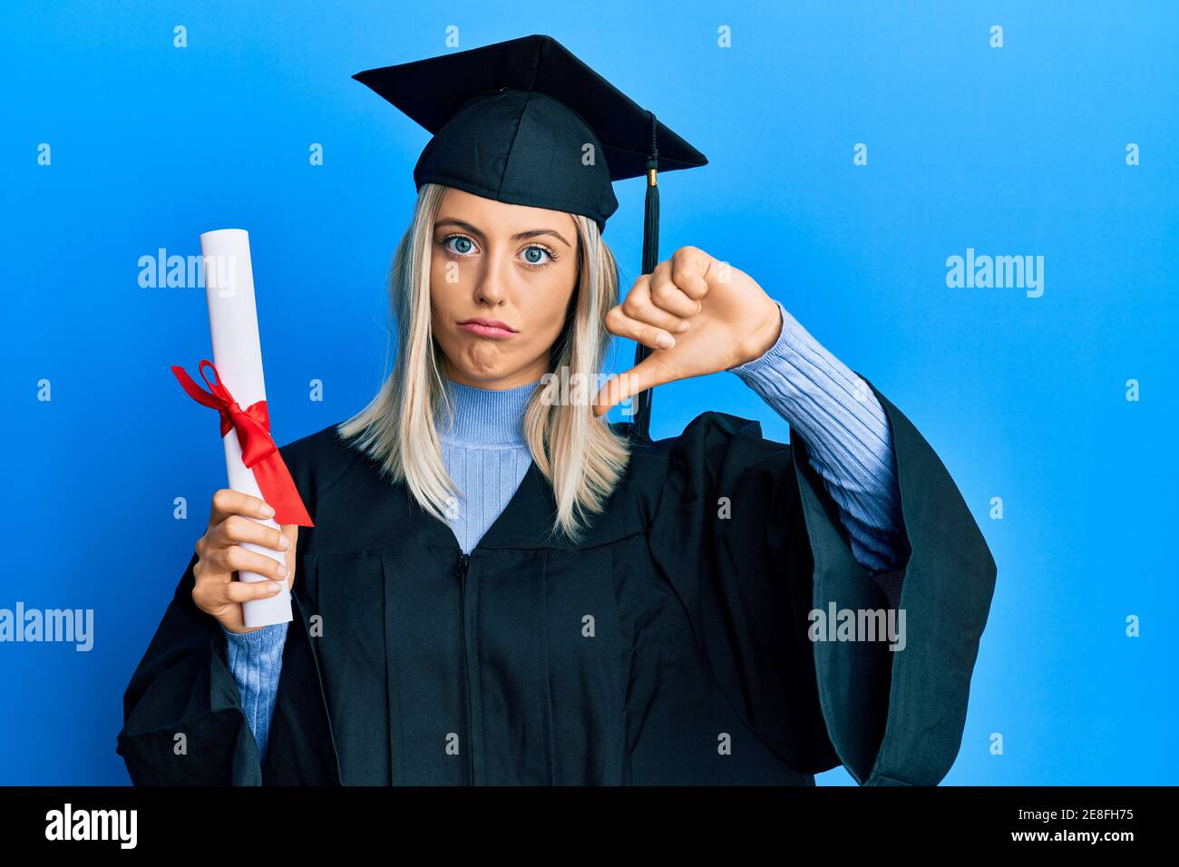 Beautiful blonde woman wearing graduation cap and ceremony robe holding ...