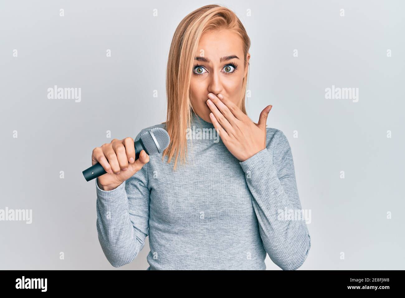 Beautiful caucasian woman singing song using microphone covering mouth ...
