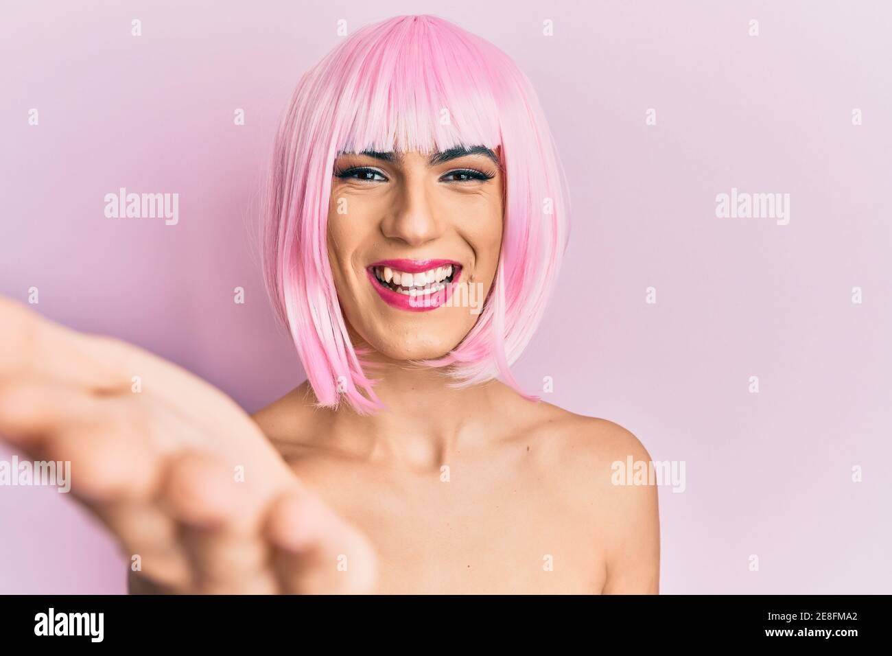 Young man wearing woman make up wearing pink wig smiling friendly ...