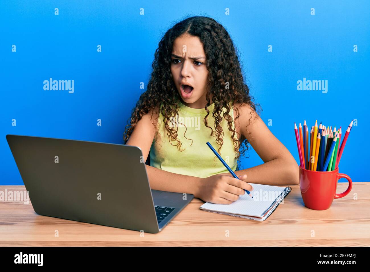 Teenager hispanic girl sitting on the table studying for school angry ...