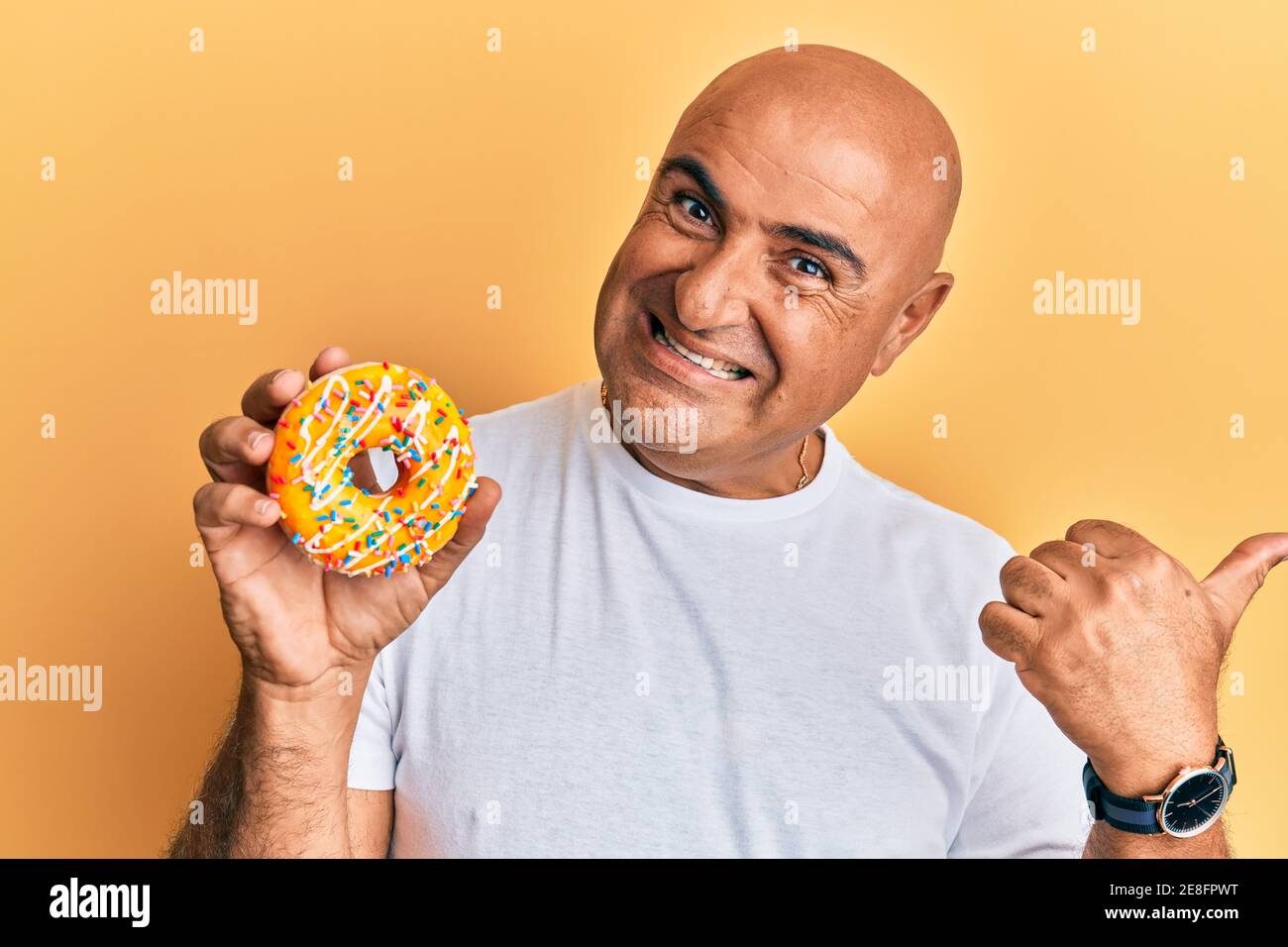 Mature middle east man holding tasty colorful doughnut pointing thumb ...