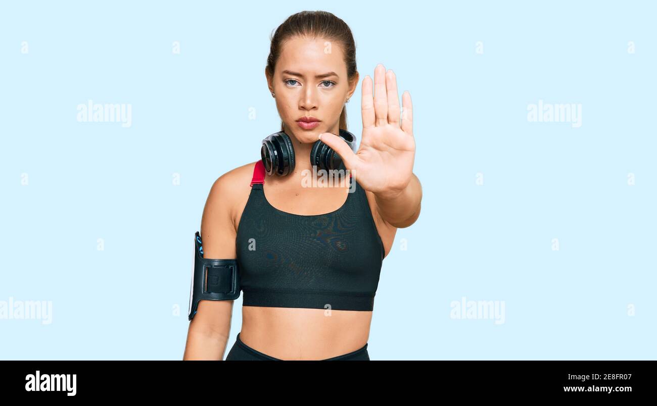 Beautiful blonde woman wearing gym clothes and using headphones doing ...