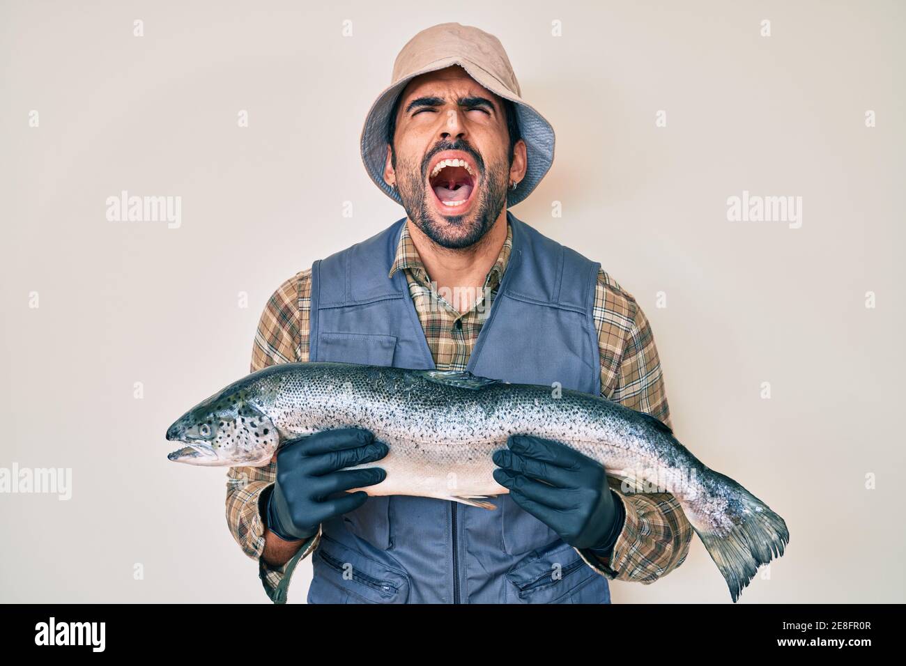 Handsome hispanic man with beard showing raw salmon angry and mad ...