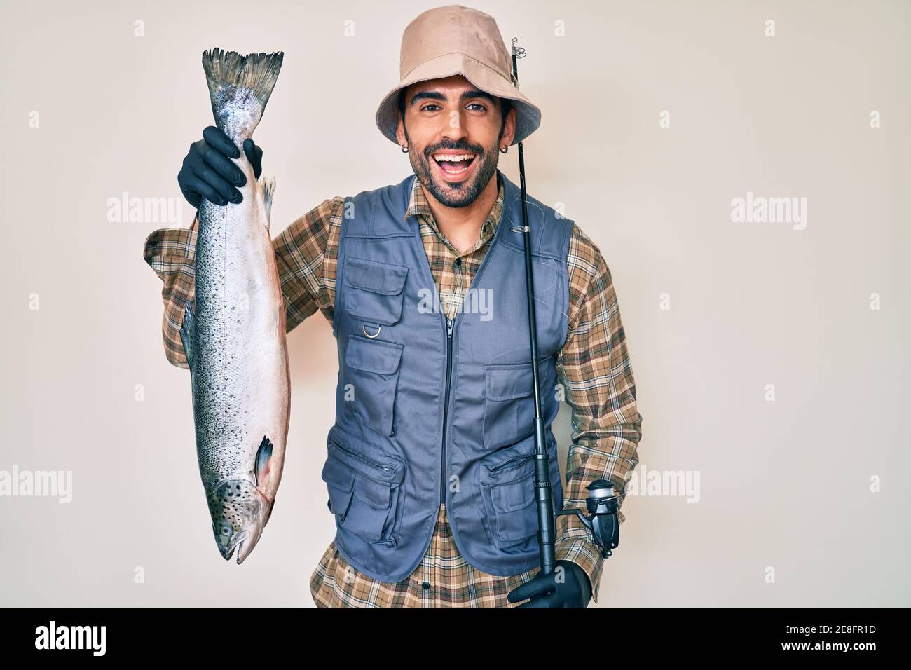 Handsome hispanic man with beard holding fishing rod and raw salmon ...