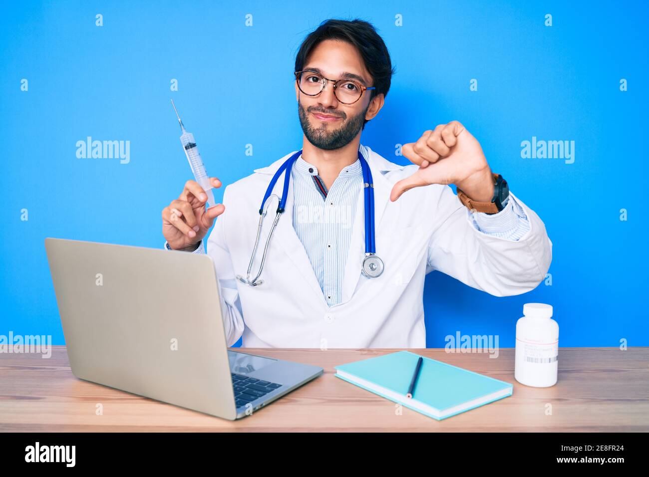 Handsome hispanic doctor man at the clinic holding syringe with angry ...