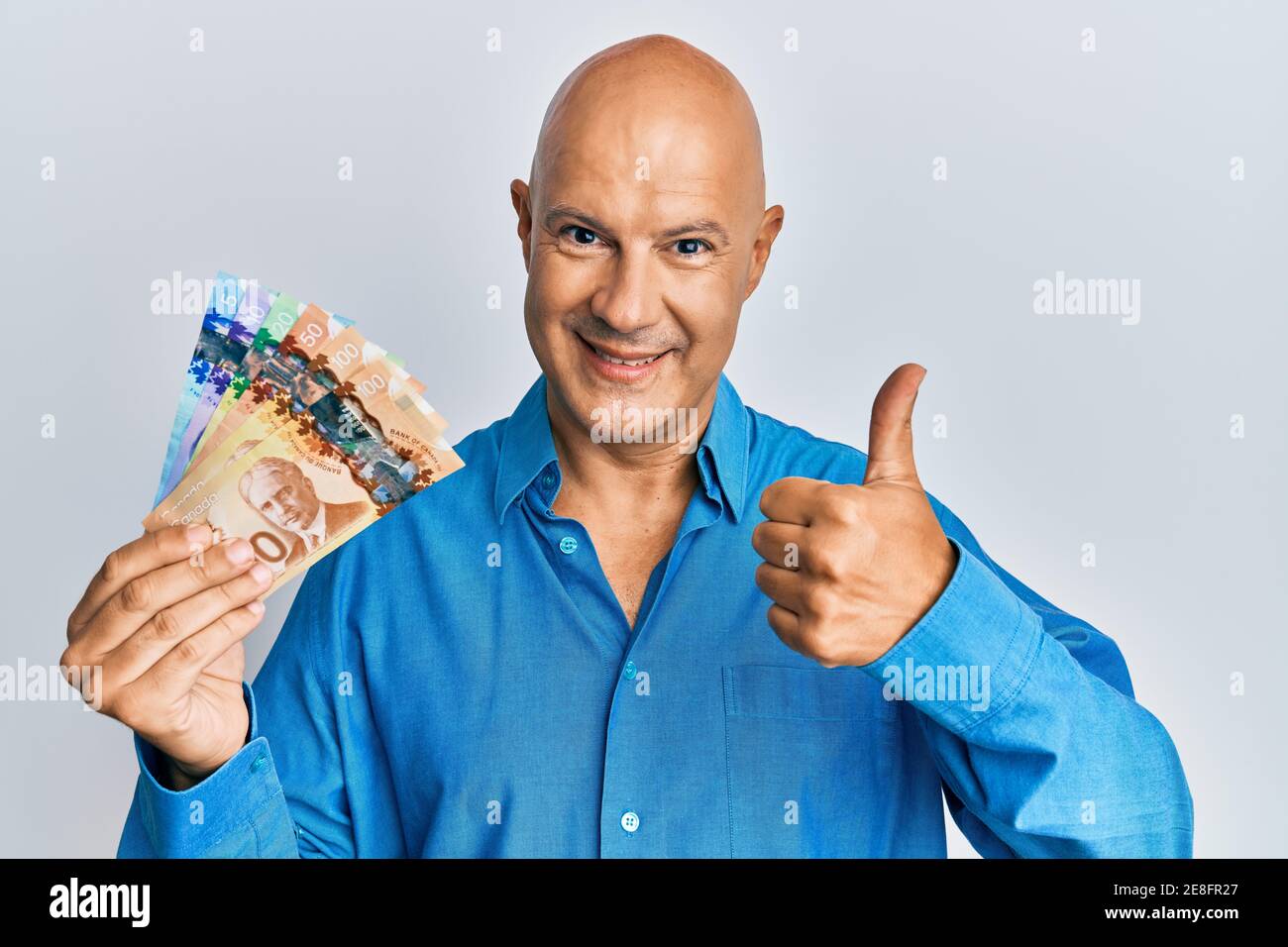 Middle age bald man holding canadian dollars smiling happy and positive ...
