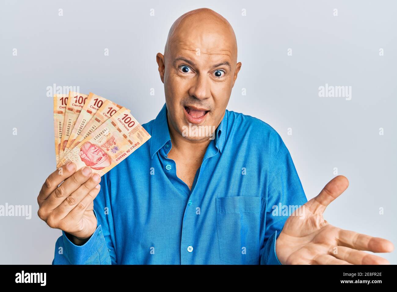 Middle age bald man holding mexican pesos celebrating achievement with ...