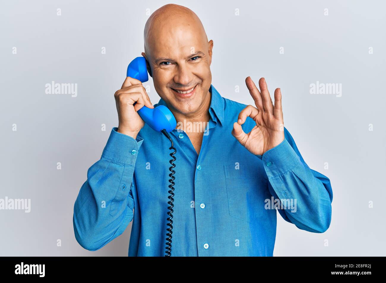 Middle age bald man speaking on vintage telephone doing ok sign with ...