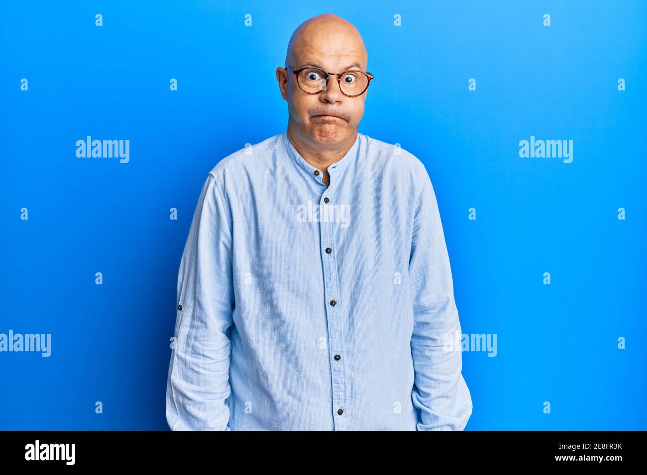 Middle age bald man wearing casual clothes and glasses puffing cheeks ...