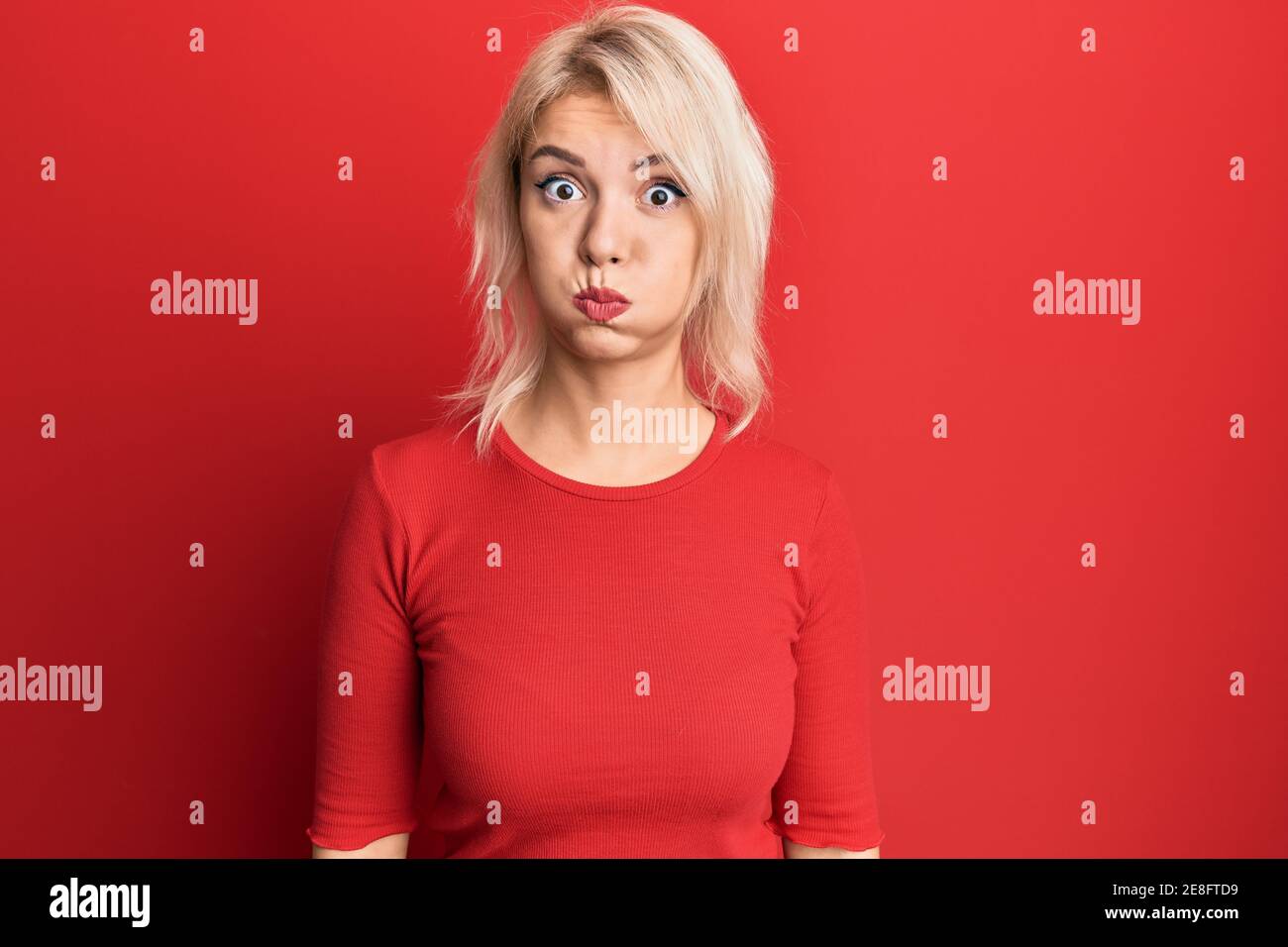 Young blonde girl wearing casual clothes puffing cheeks with funny face ...